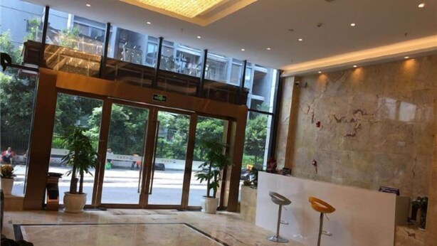 Um hall de hotel com entrada de vidro, plantas em vasos e um balcão de recepção.
