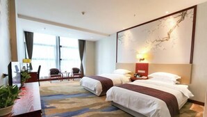 Quarto de hotel com duas camas, uma escrivaninha, uma cadeira, uma janela grande e uma obra de arte na parede.