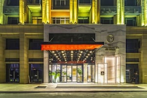 Entrada de hotel com marquise vermelha marcante, porta de vidro grande e placa com logotipo.