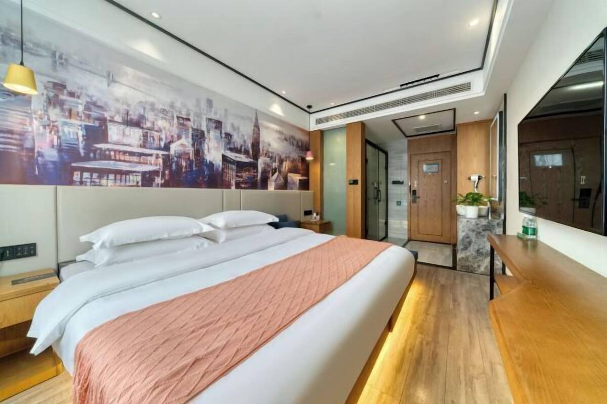 Quarto de hotel moderno com uma cama grande, uma escrivaninha de madeira e um mural com vista para a cidade.