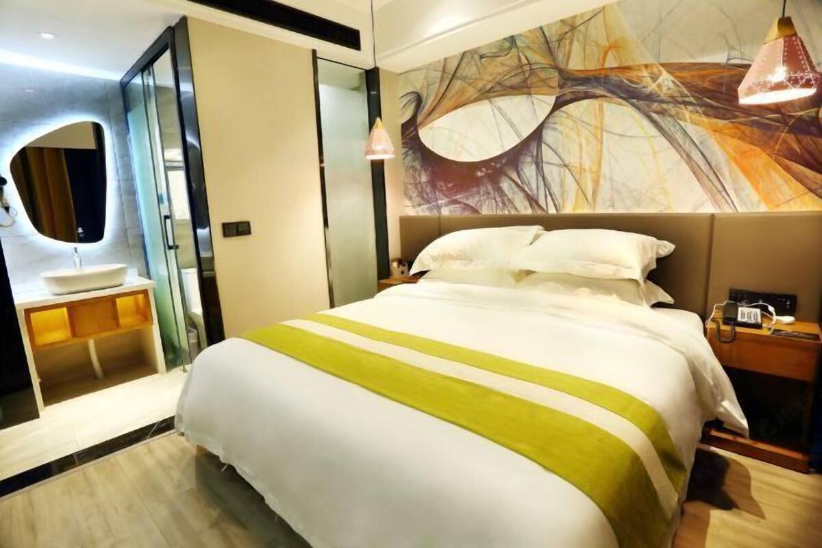 Quarto de hotel com cama, mesa de cabeceira, espelho e uma parede com arte abstrata.