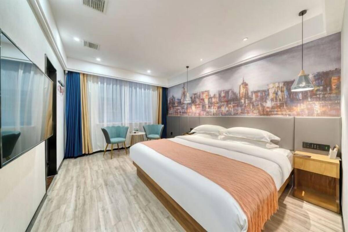 Quarto de hotel com uma cama grande, um mural da paisagem urbana, uma escrivaninha com uma luminária e uma TV na parede esquerda.