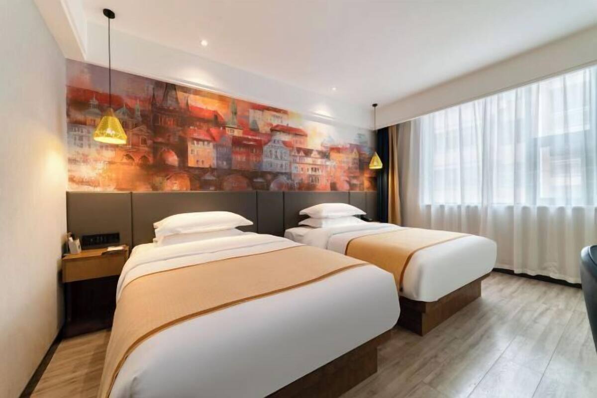 Quarto de hotel com duas camas, um mural grande com vista para a cidade e uma janela com cortinas leves.