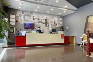 Uma área de recepção com uma mesa vermelha, um monitor e um mural com vista para a cidade na parede.