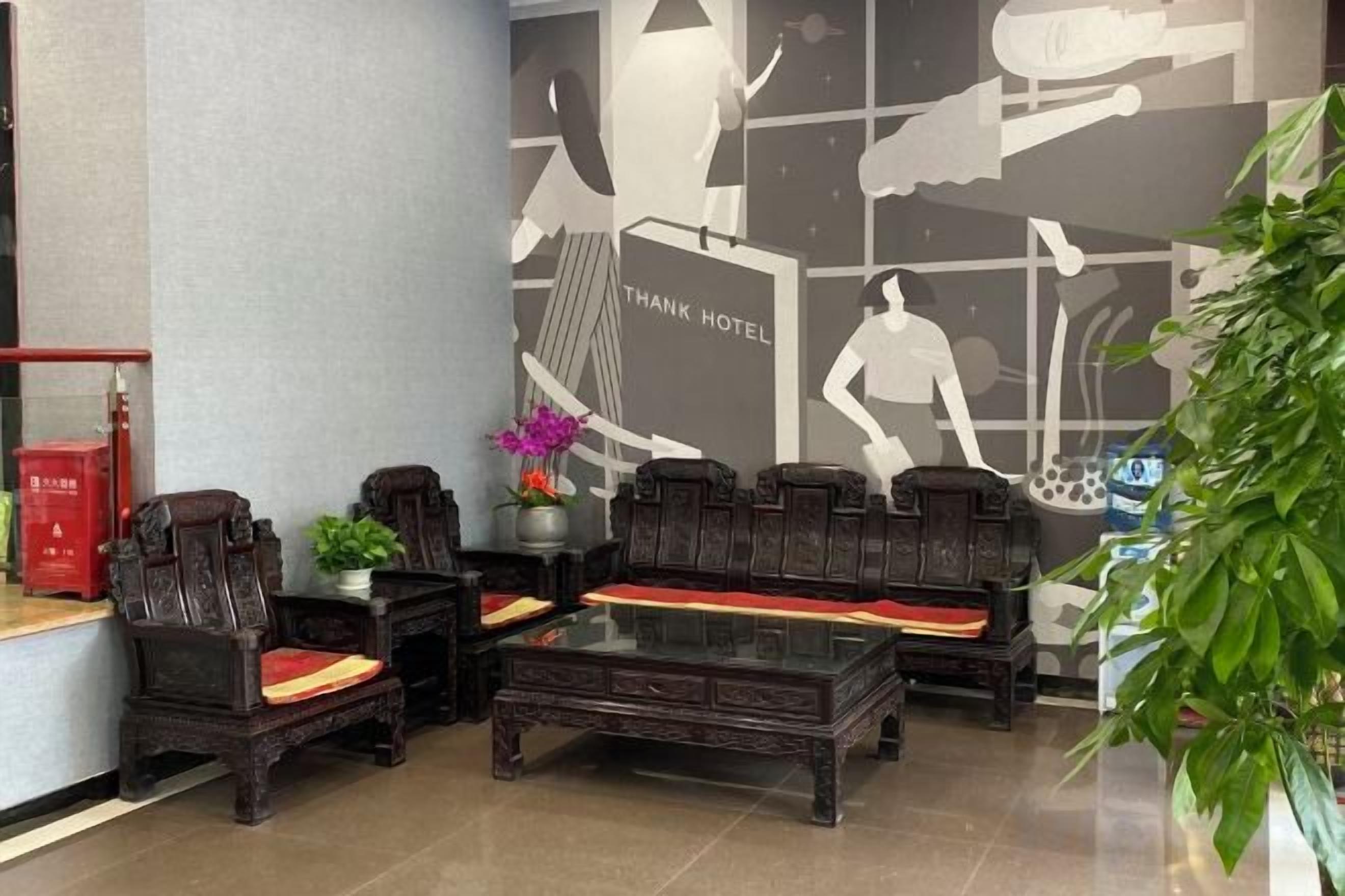 Um saguão com balcão de recepção, área de estar com cadeiras e uma mesa, e uma parede com o letreiro 'THANK HOTEL'.