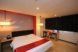 Quarto de hotel com cama, escrivaninha, cadeira e uma janela grande com cortinas.