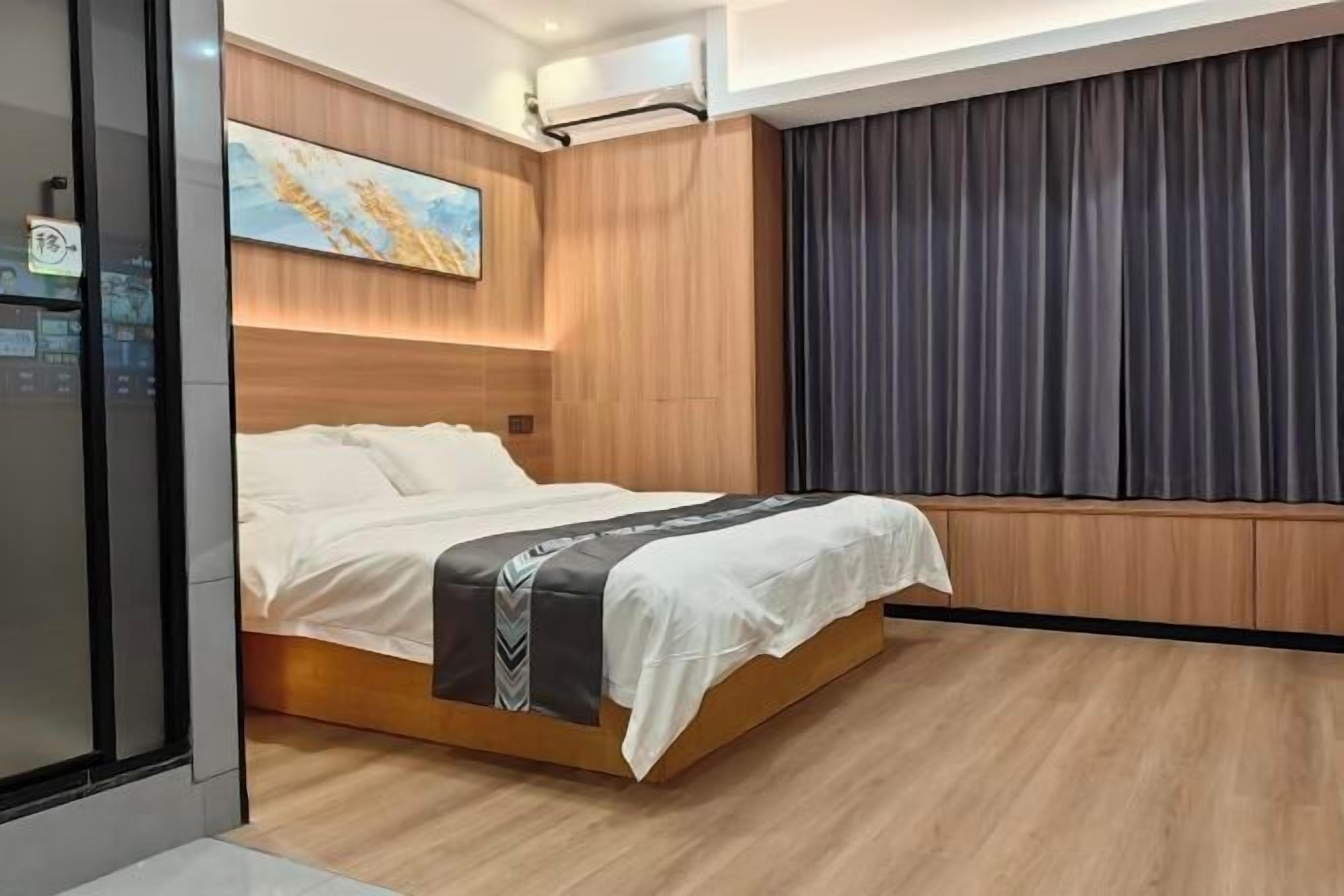 Quarto de hotel com cama, um quadro na parede, janela com cortinas e ar condicionado.