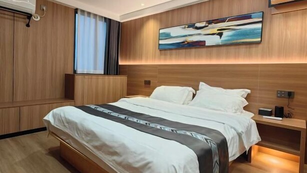 Quarto moderno com cama grande, painéis de madeira, pintura na parede e mesa de cabeceira com abajur.