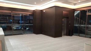 Um lobby moderno com elevador de vidro, balcão de recepção e vista para carros estacionados lá fora.