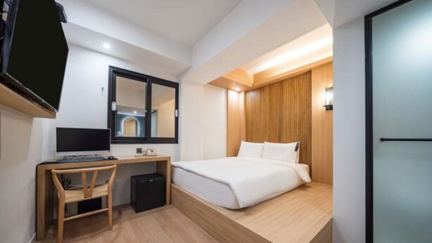 Quarto de hotel moderno com cama, escrivaninha, cadeira e um pequeno frigorífico.