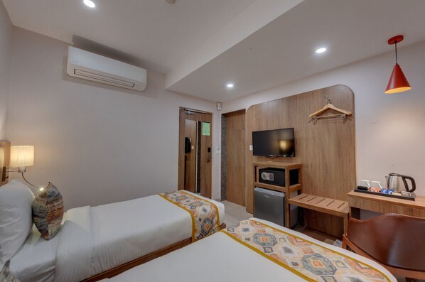 Quarto de hotel com duas camas, televisão, secretária com chaleira e guarda-roupa de madeira.