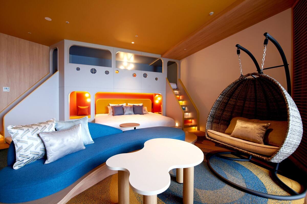 Quarto moderno com cama, cadeira suspensa e um espaço de estar diferenciado.