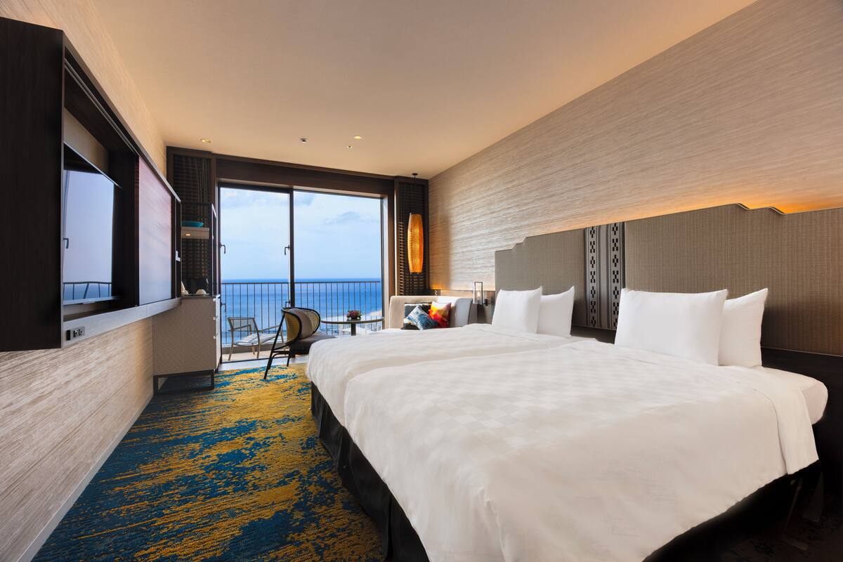 Quarto de hotel com cama grande, escrivaninha, cadeira e vista para o oceano.
