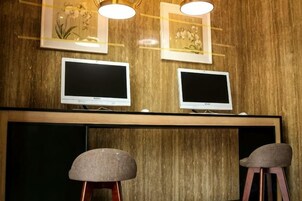 Quarto com dois monitores em uma parede de madeira, um quadro-negro abaixo e dois banquinhos.