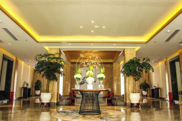 Um hall de hotel com uma fonte central, plantas em vasos e piso lustroso.