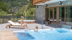 Uma piscina com espreguiçadeiras, uma banheira de hidromassagem e um muro de pedra.