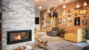 Uma sala de estar aconchegante com lareira, assentos confortáveis e uma parede decorada com diversas fotos emolduradas e uma cabeça de alce.