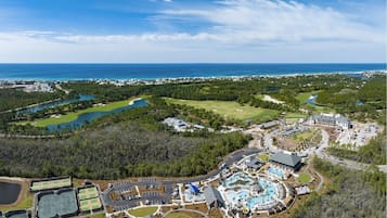Vista aérea de um resort com uma piscina grande, campos de golfe e vista para o oceano.