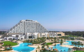 Um hotel moderno com um edifício em formato de pirâmide singular, várias piscinas e jardins bem cuidados.