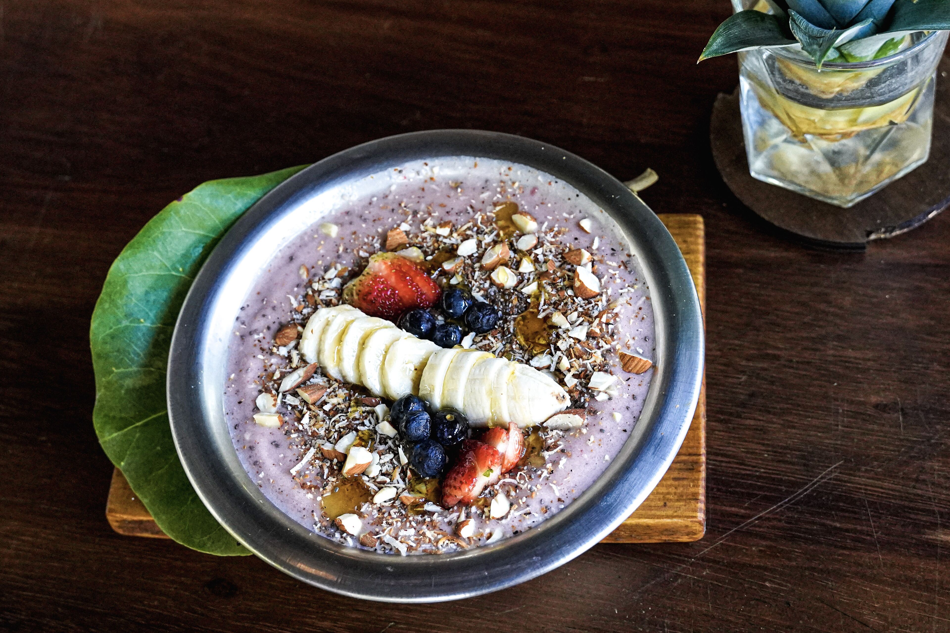 Uma taça de smoothie com frutas e nozes sobre uma tábua de madeira.