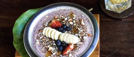 Uma taça de smoothie com frutas e nozes sobre uma tábua de madeira.