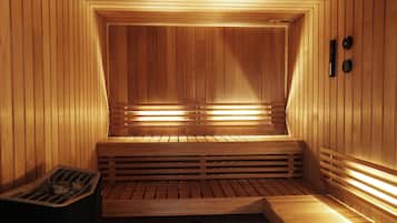 Uma sauna com bancos de madeira e um banco no chão, uma lixeira e dois controles fixados na parede.
