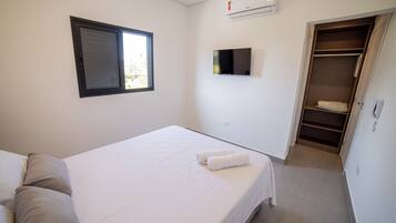 Um quarto com uma cama, uma televisão, um ar condicionado e um guarda-roupa.
