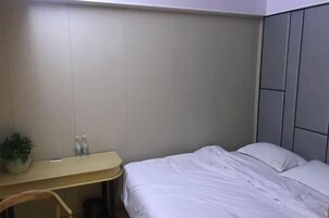 Quarto de hotel com cama, escrivaninha e planta em vaso.