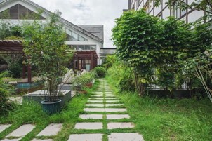 Um caminho no jardim leva a um edifício moderno com pérgola e vegetação exuberante.