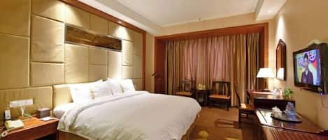 Quarto de hotel com uma cama grande, uma escrivaninha com cadeira, televisão e janela com cortinas.