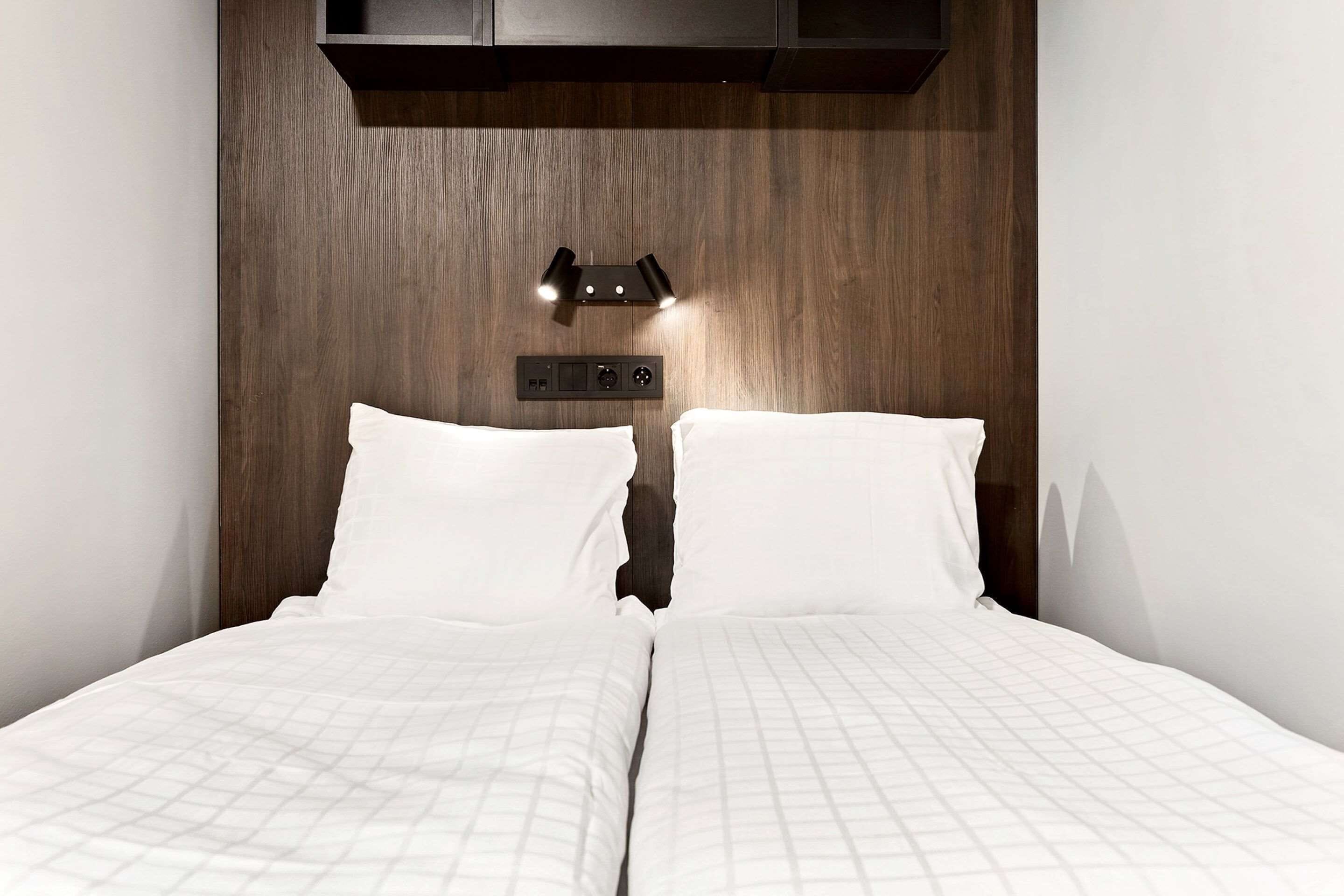 Cama de casal com roupa de cama branca e cabeceira de madeira.
