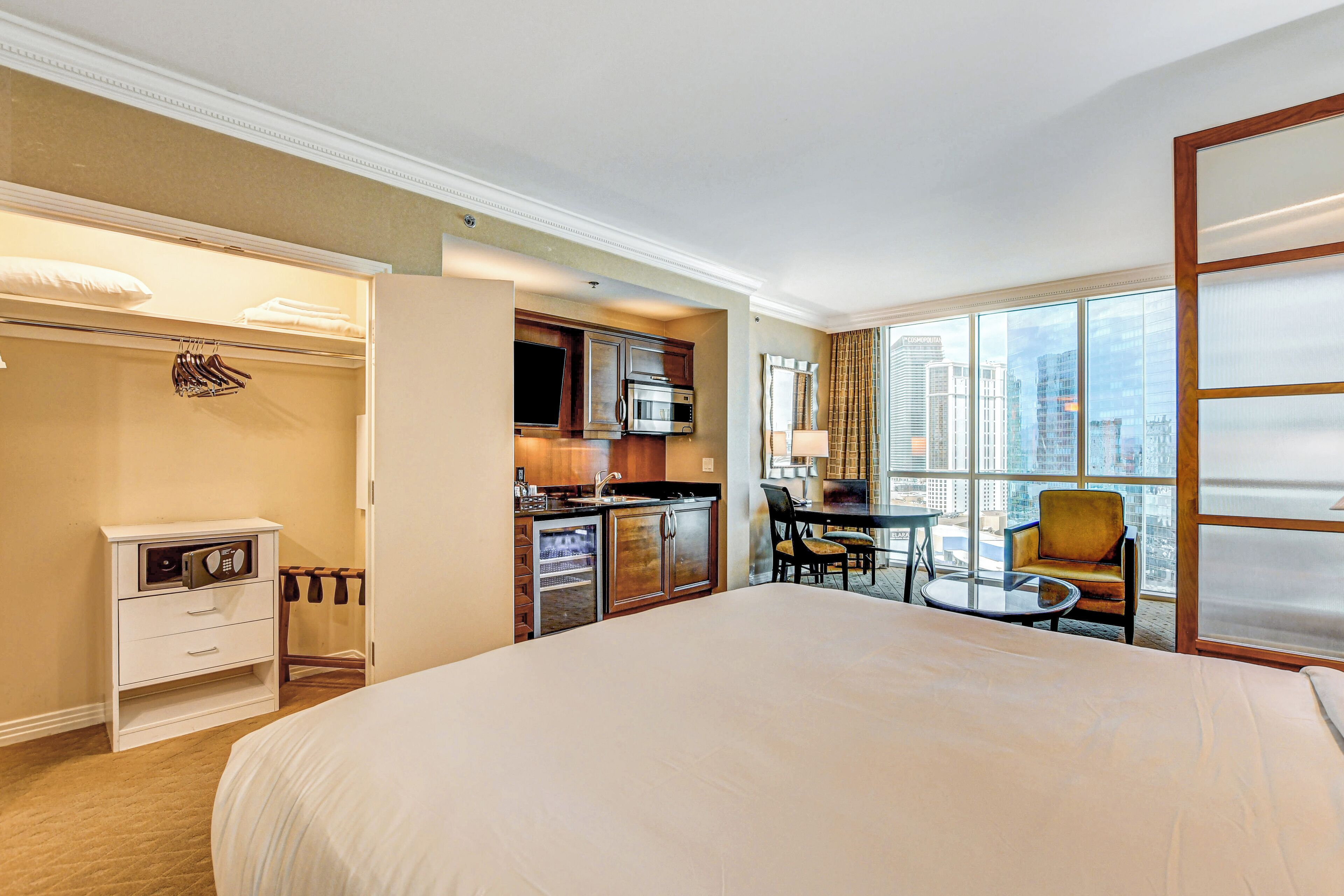 Quarto de hotel com cama grande, cozinha compacta, área de refeições e vista da cidade.