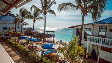 Um hotel à beira-mar com área de piscina, guarda-sóis e palmeiras.