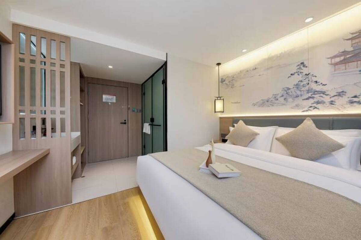 Quarto de hotel com uma cama, uma escrivaninha e uma parede com um quadro.