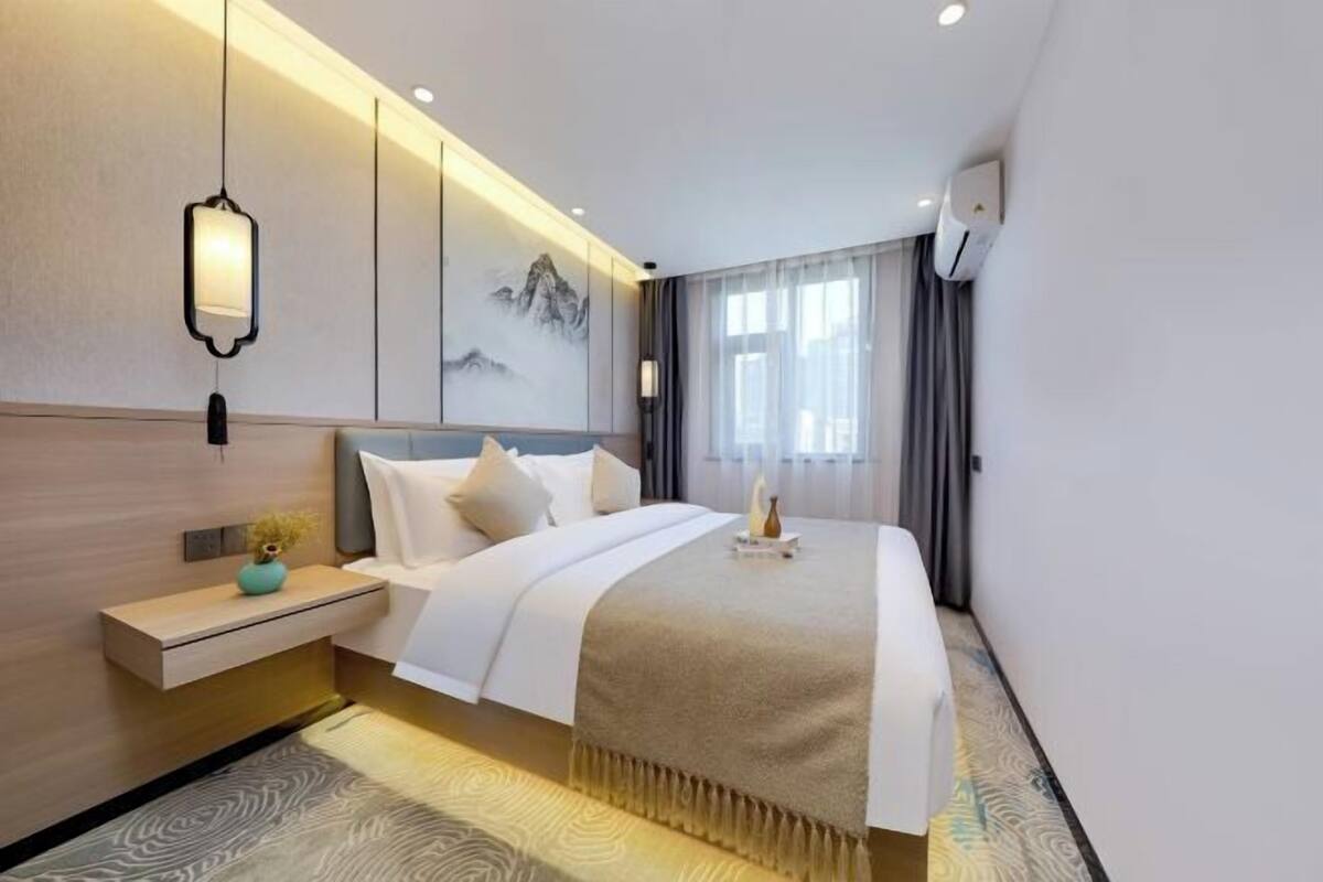 Quarto de hotel moderno com cama, mesa de cabeceira, obras de arte na parede e janela com cortinas.