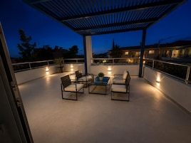 Um terraço ao ar livre com pérgola, área de estar e plantas em vasos.