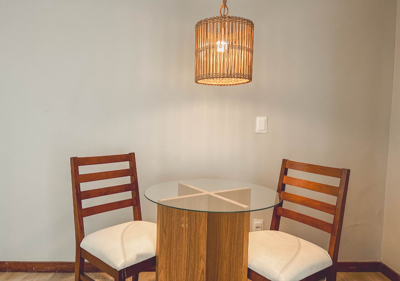 Uma área de refeições com duas cadeiras de madeira e uma mesa redonda de vidro.