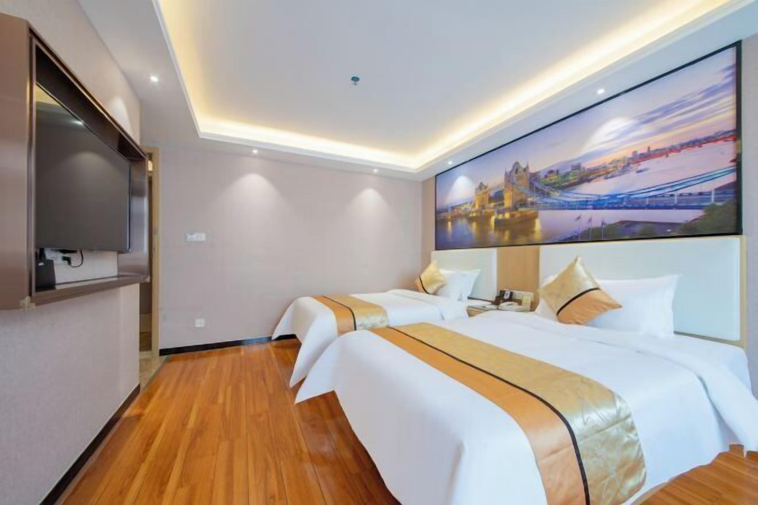 Quarto de hotel com duas camas, televisão de tela plana e uma grande pintura de paisagem urbana.