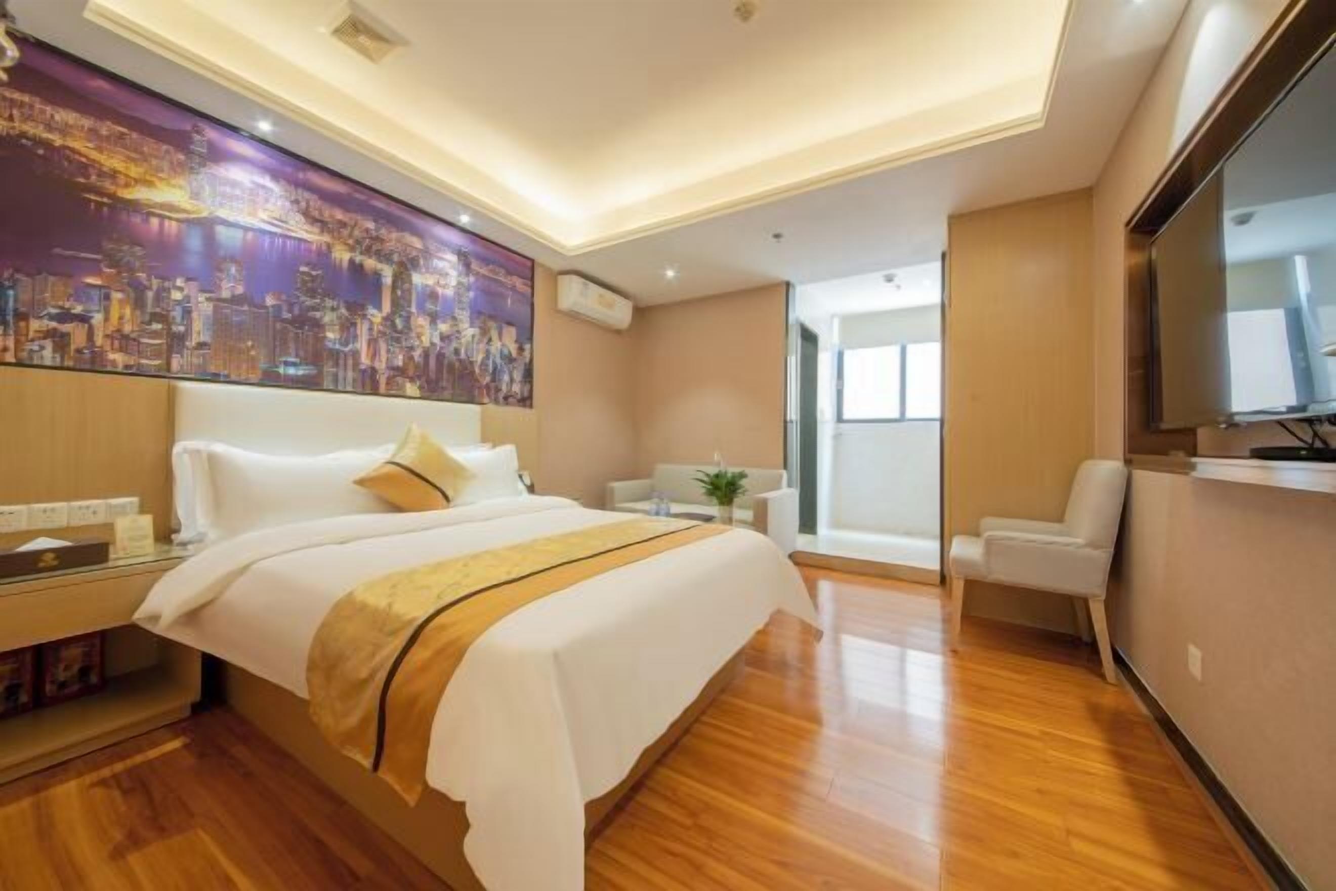 Quarto de hotel moderno com uma cama grande, televisão de tela plana, escrivaninha com cadeira e uma pintura com vista para a cidade.
