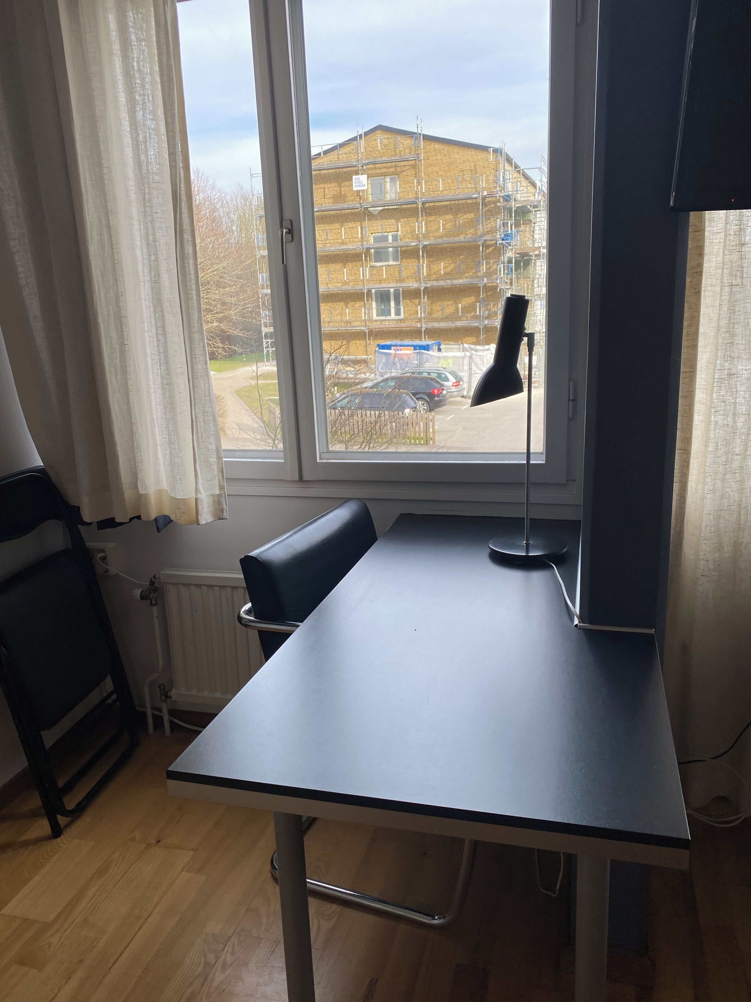 Um quarto com uma janela grande, uma mesa, uma cadeira e um abajur.