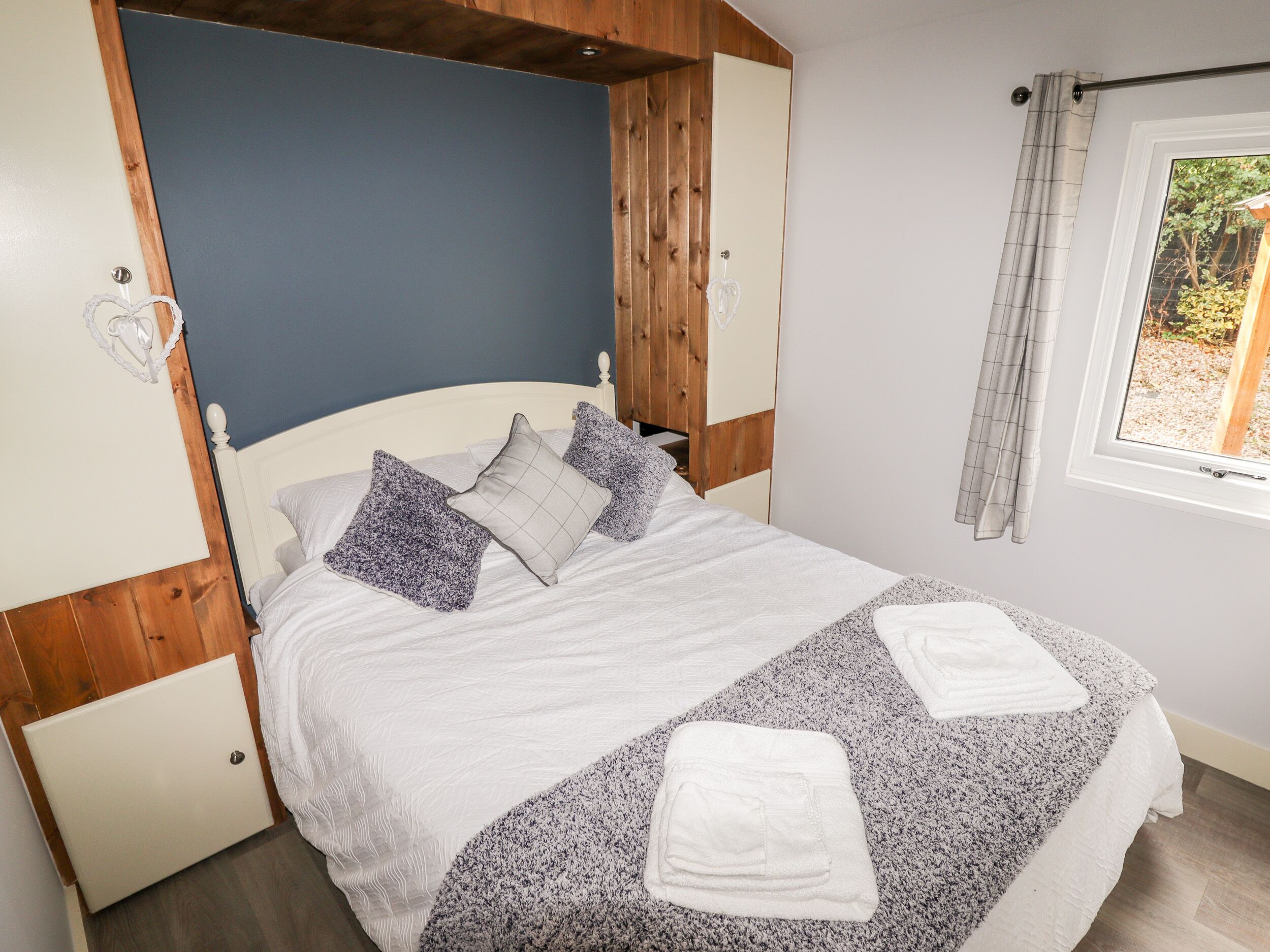 Quarto com cama, travesseiros, janela com cortinas e vista para o verde lá fora.