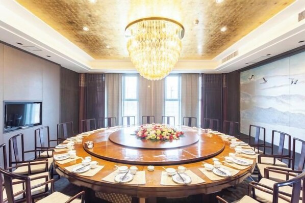 Uma sala de conferências com uma mesa redonda, cadeiras, um lustre e uma janela ampla.