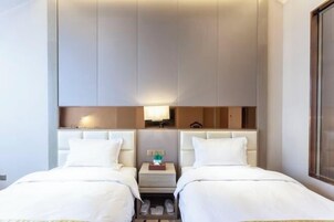 Quarto de hotel com duas camas, uma mesa de cabeceira com abajur e um guarda-roupa espaçoso.
