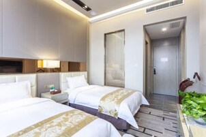 Quarto de hotel com duas camas, uma mesa de cabeceira com abajur, um espelho e uma porta que dá para outro cômodo.
