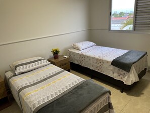 Quarto com duas camas de solteiro, uma mesa de cabeceira com um vaso de flores e uma janela com vista para edifícios.