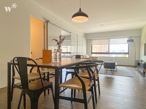 Uma sala de jantar moderna com uma mesa e cadeiras de madeira, uma luminária pendente e vista da cidade por grandes janelas.