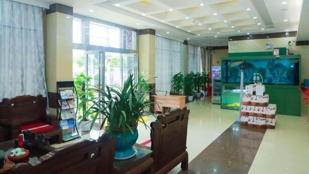 Um hall de hotel com mobiliário de madeira, uma grande planta em vaso, um balcão de recepção e um aquário.