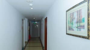 Um corredor com um quadro na parede, piso de azulejos e uma porta no final.