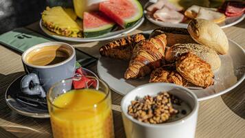 Uma mesa de pequeno-almoço com croissants, pão, fruta e uma chávena de café.
