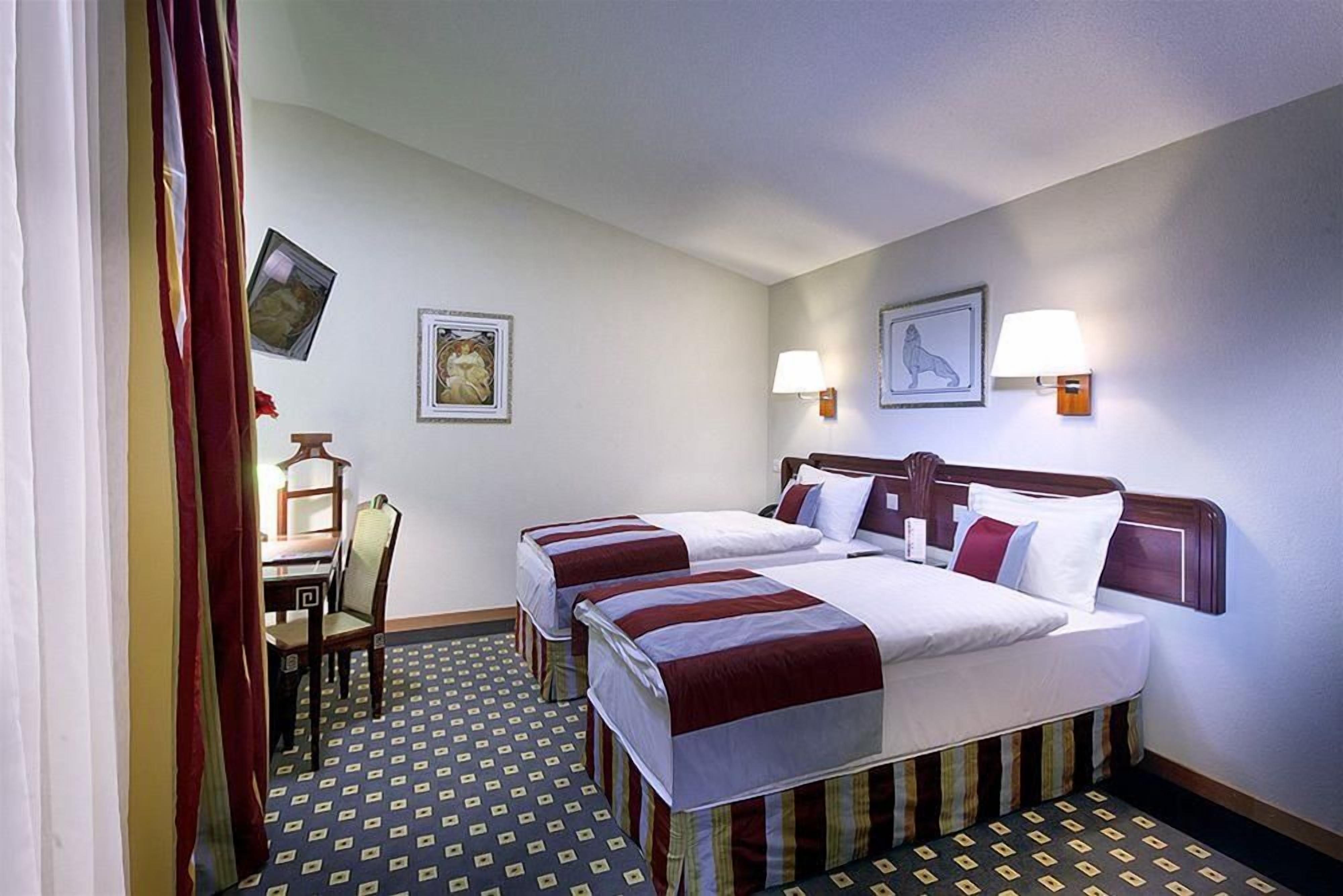 Quarto de hotel com duas camas, uma escrivaninha e cadeiras.